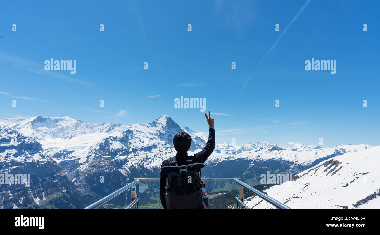 a man with backpack raising hand up with Swiss Alpine mountains view in ...