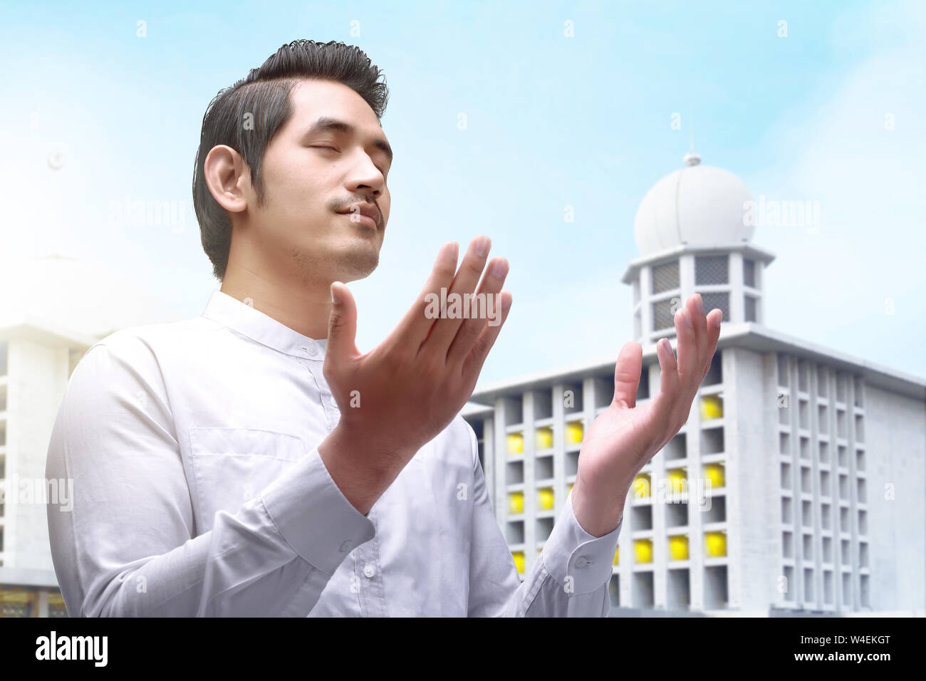 Asian Muslim man standing and praying while raised arms outside the ...