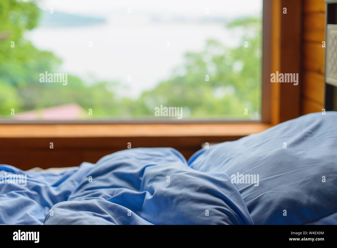 Bed with blue linen in front of the window with blurred nature view in ...