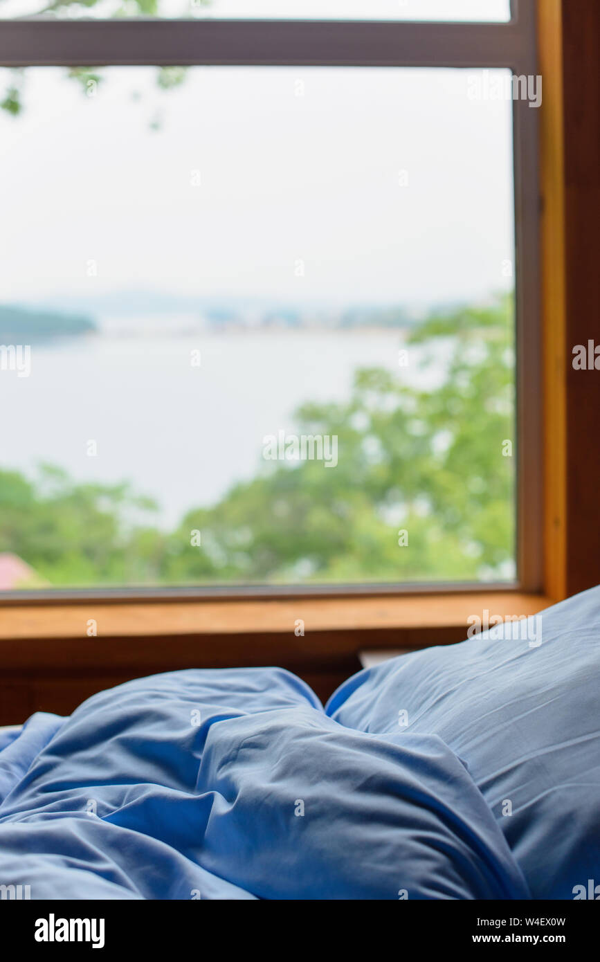 Bed with blue linen in front of the window with blurred nature view in ...
