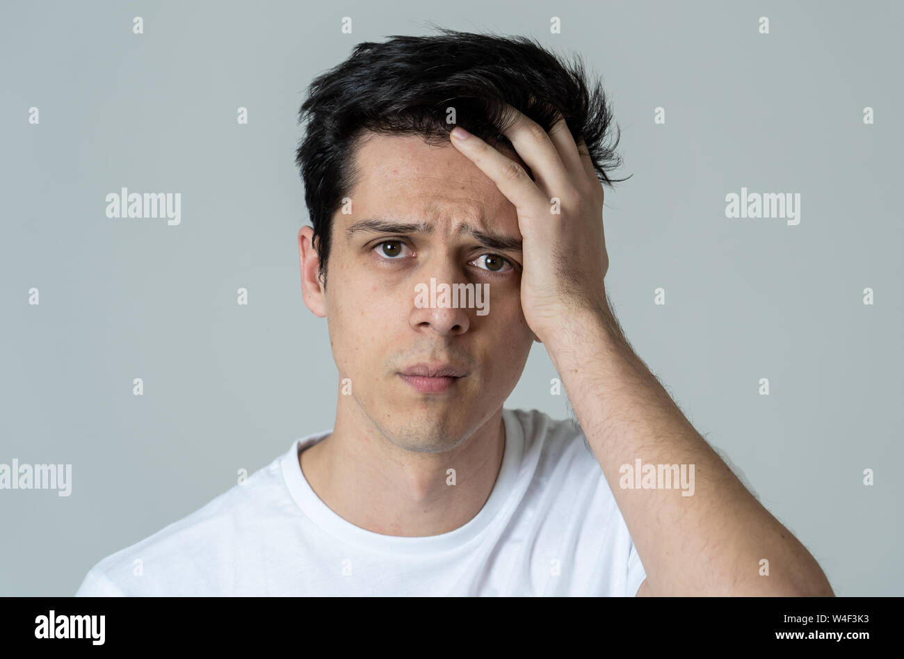 Close up of a young sad man, serious and concerned, looking worried and thoughtful. Touching her ...