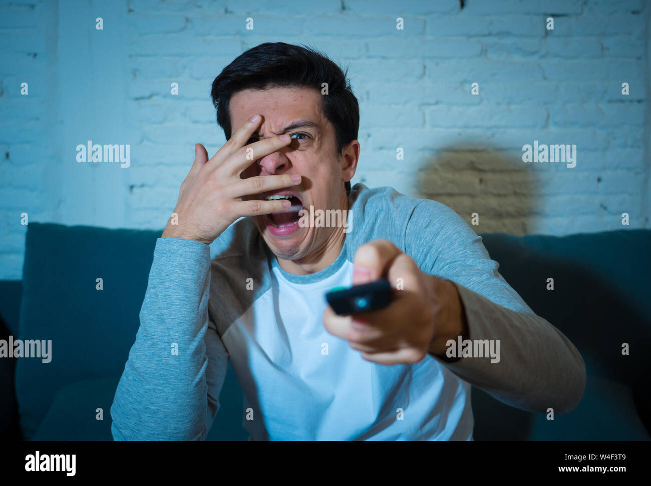 Lifestyle portrait of young scared man watching horror movie or ...