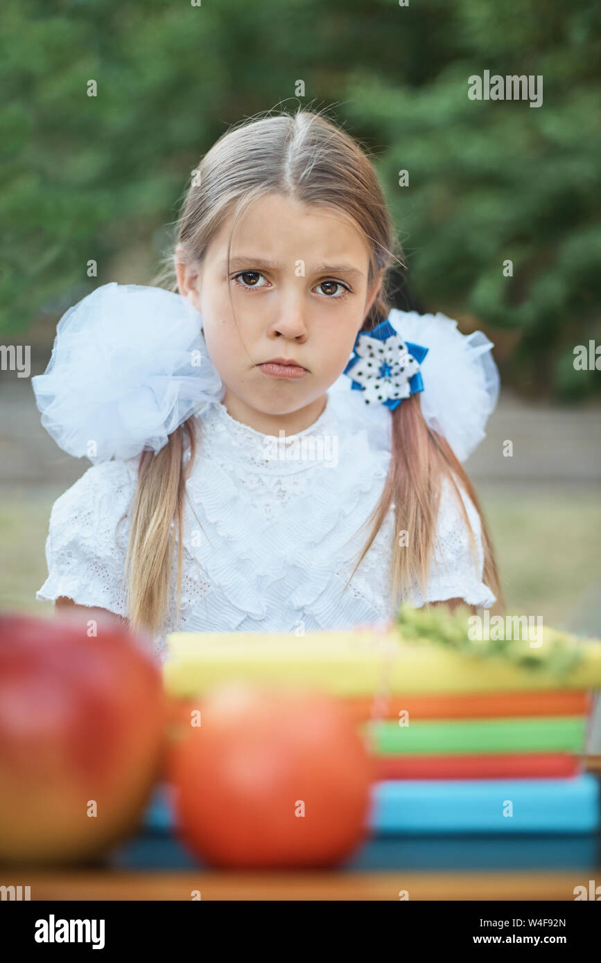 Portrait of sad first-grader sitting at a desk on the background school ...