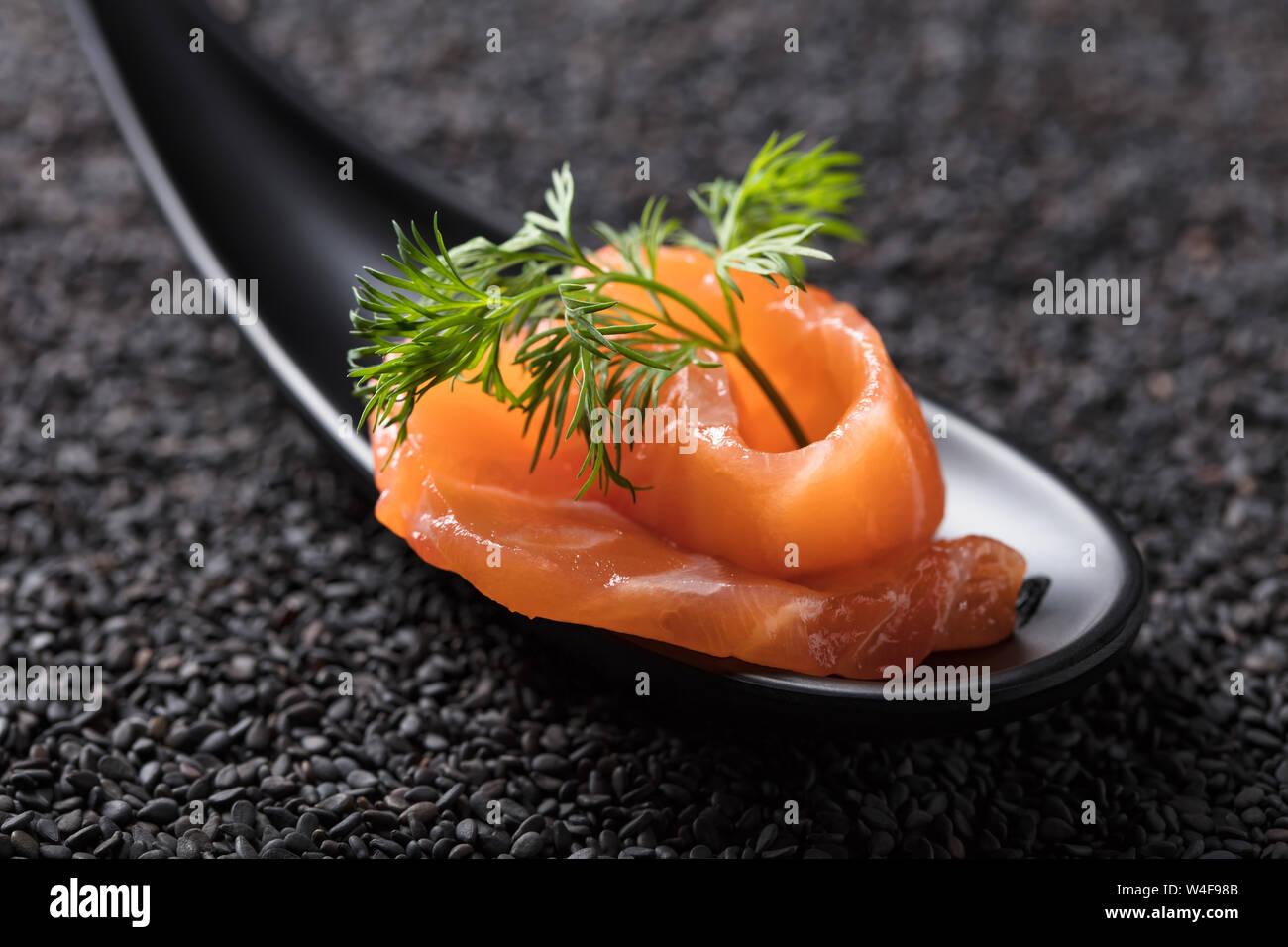 Slice of salted salmon with dill on the background of black sesame ...