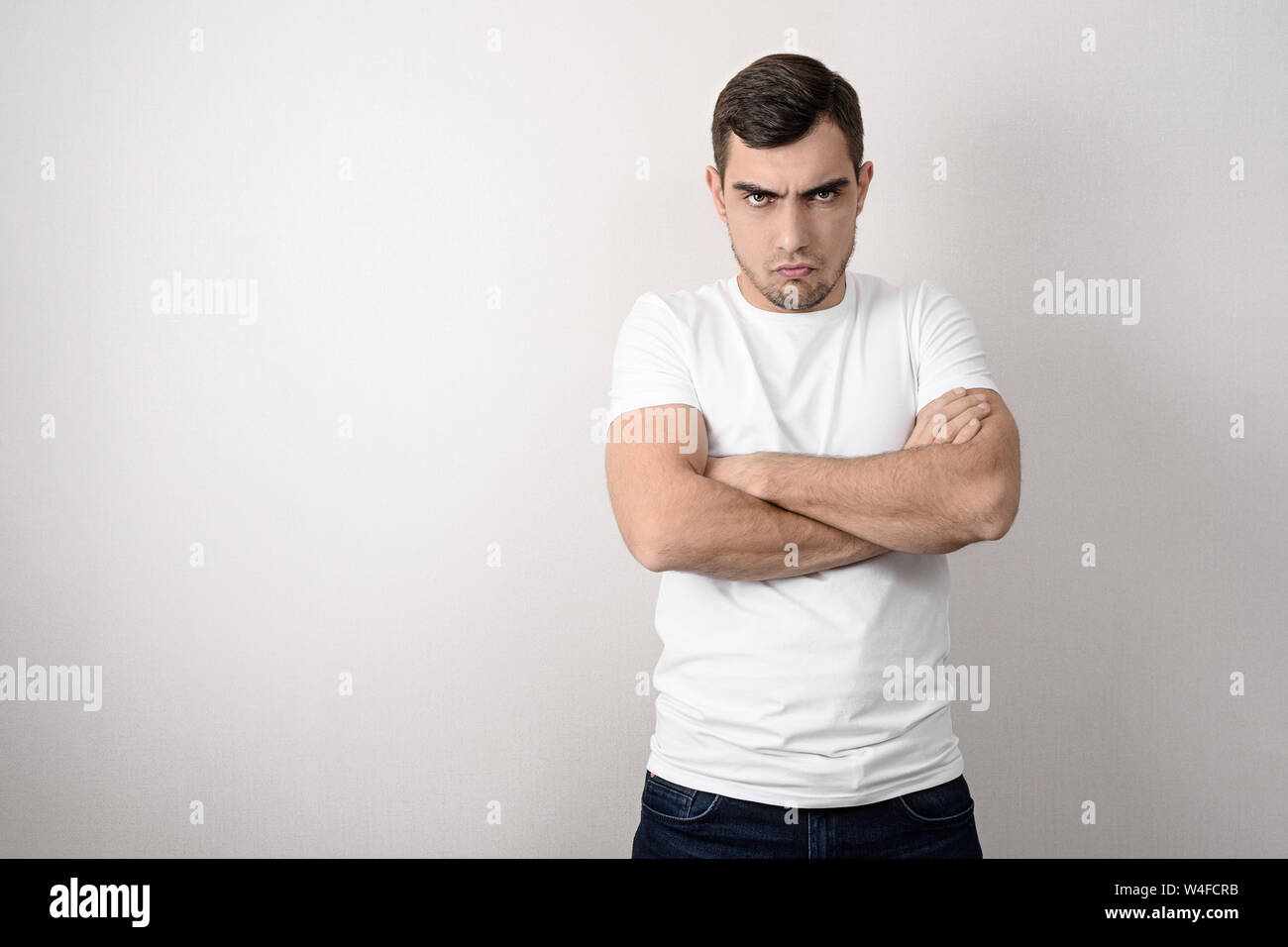 Portrait of serious, angry young man with folded arms in white t-shirt ...