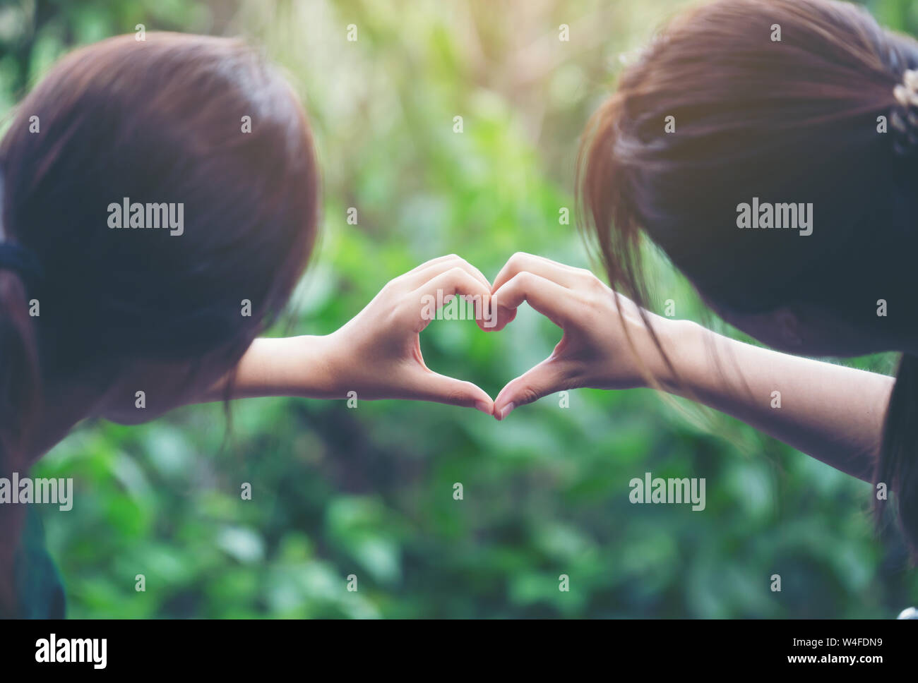 women making heart shapes with their hands on nature green background ...