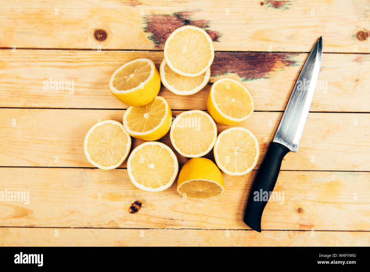 Top view of bright yellow cut lemons with knife on wooden table ...