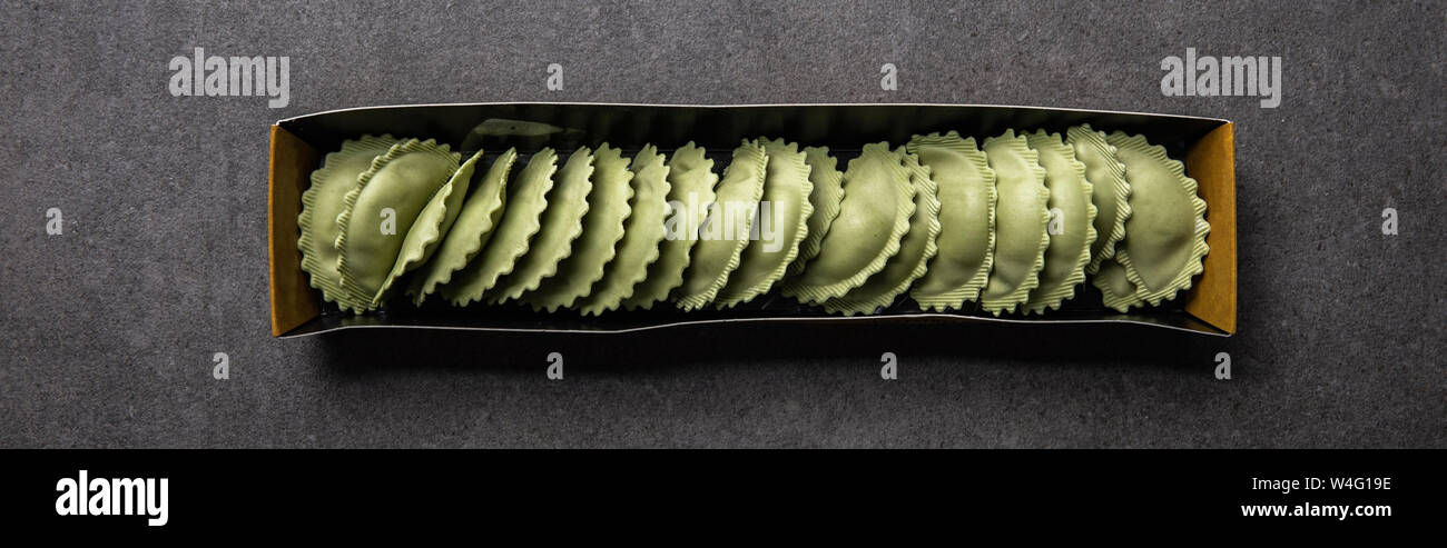top view of green raw ravioli in cardboard box on grey textured surface ...