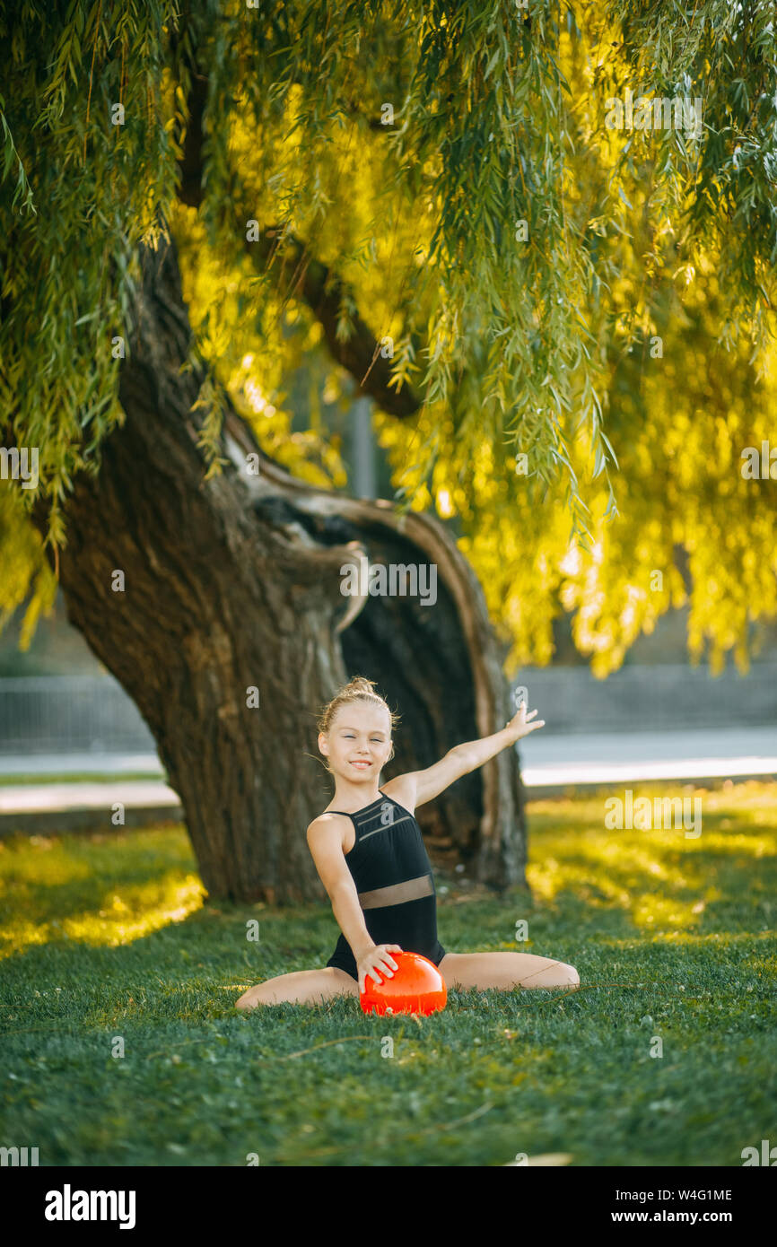Girl gymnast performs an exercise with a ball on the lawn in the park ...