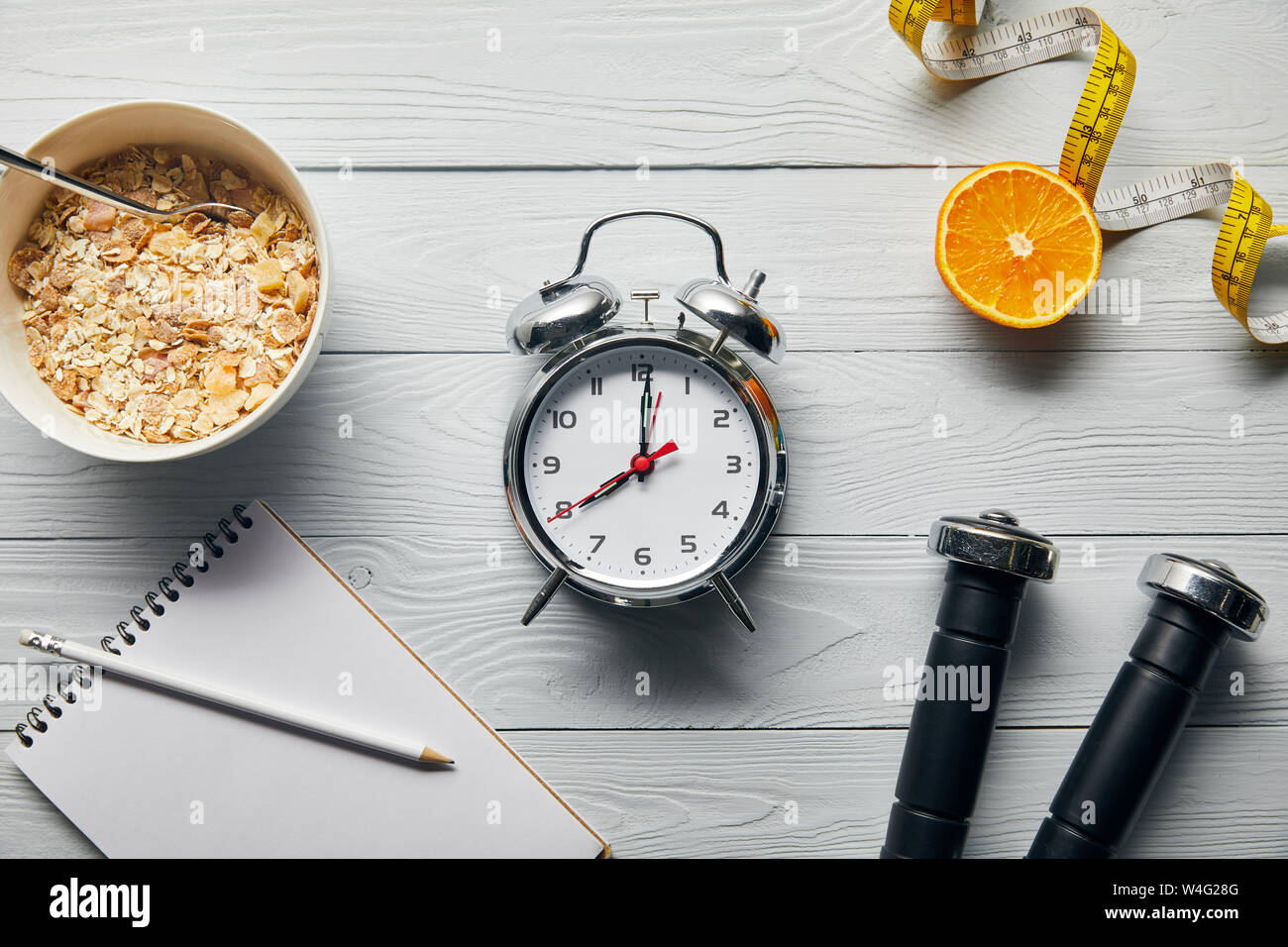 top view of silver alarm clock, notebook with pencil, breakfast cereal ...