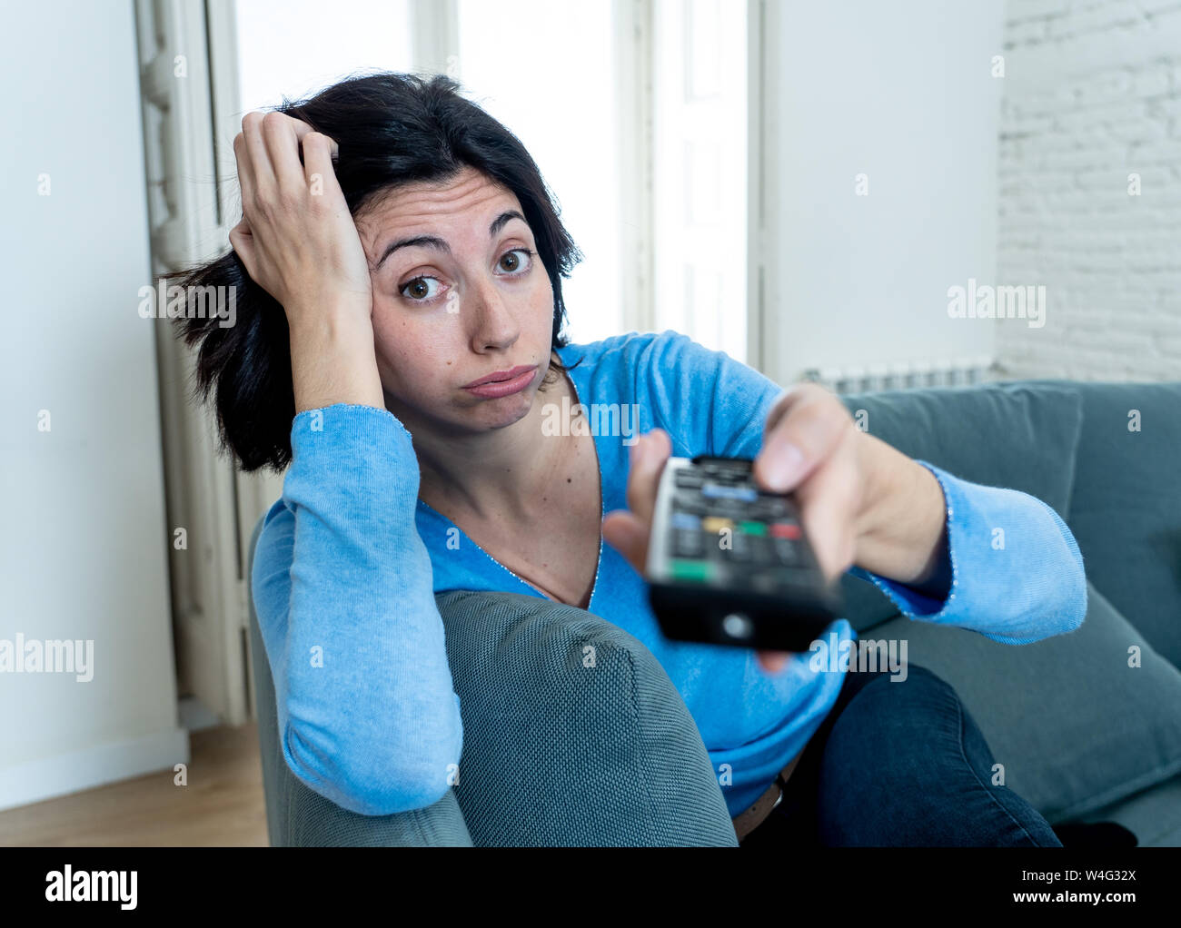 Young upset woman on sofa using control remote zapping bored of bad TV ...