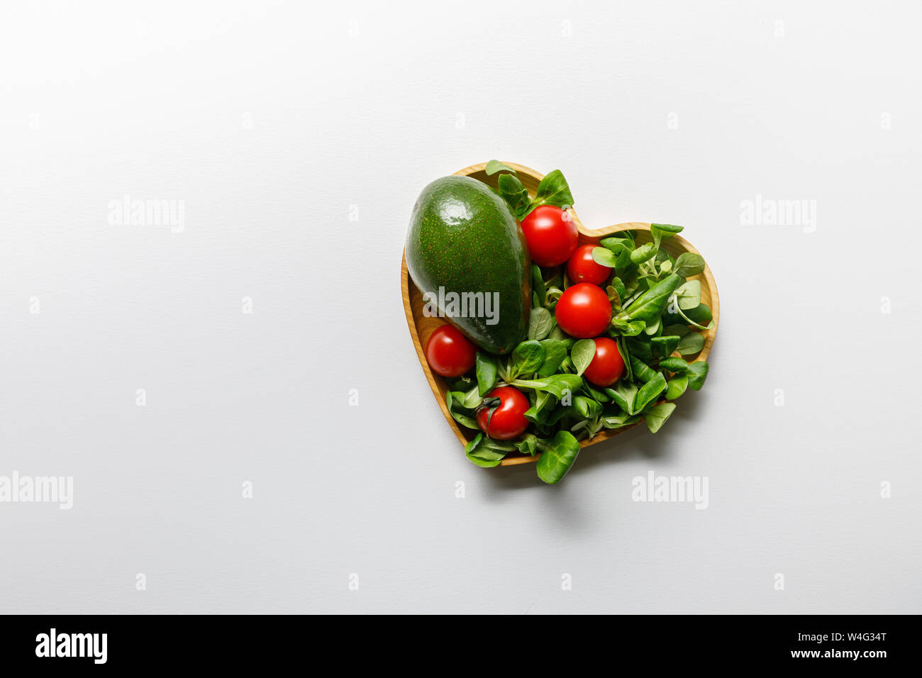 top view of fresh green vegetables in heart shaped bowl on white ...