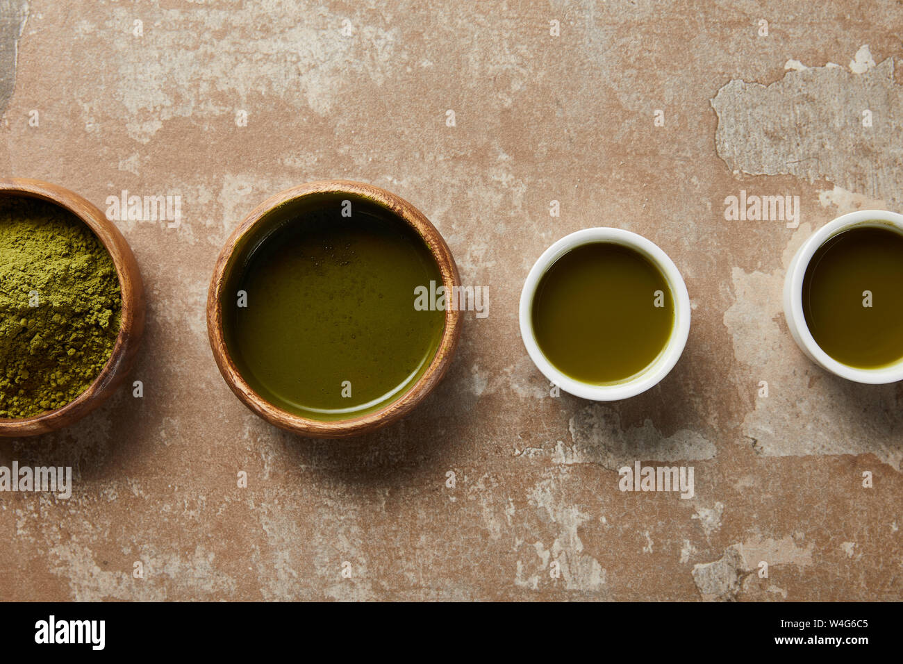 top view of matcha powder, bowl and cups with green tea on aged surface ...
