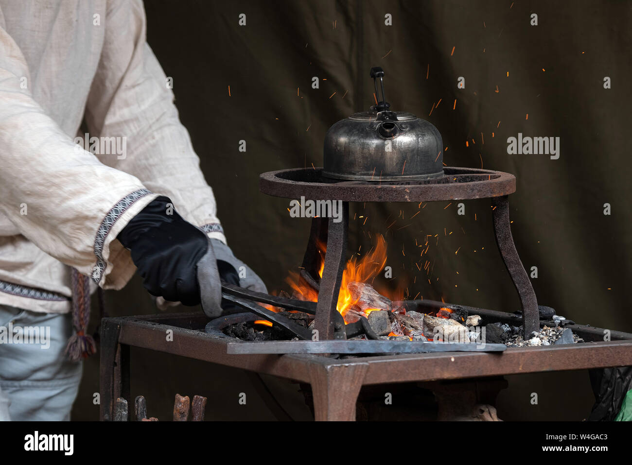 Blacksmith heating up metal in red hot coals while tea pot boiling ...
