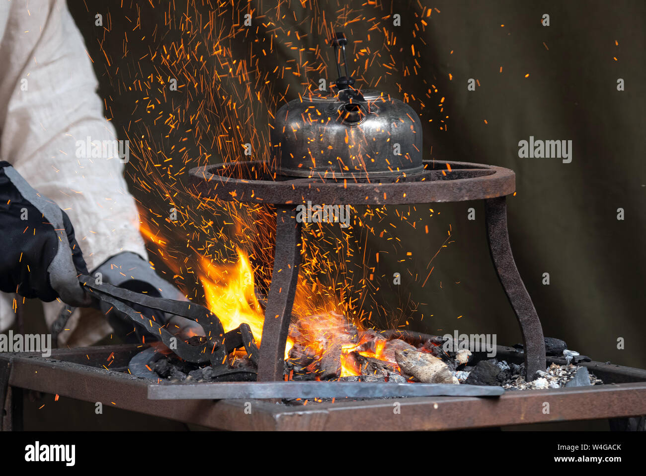 Blacksmith heating up metal in red hot coals while tea pot boiling ...