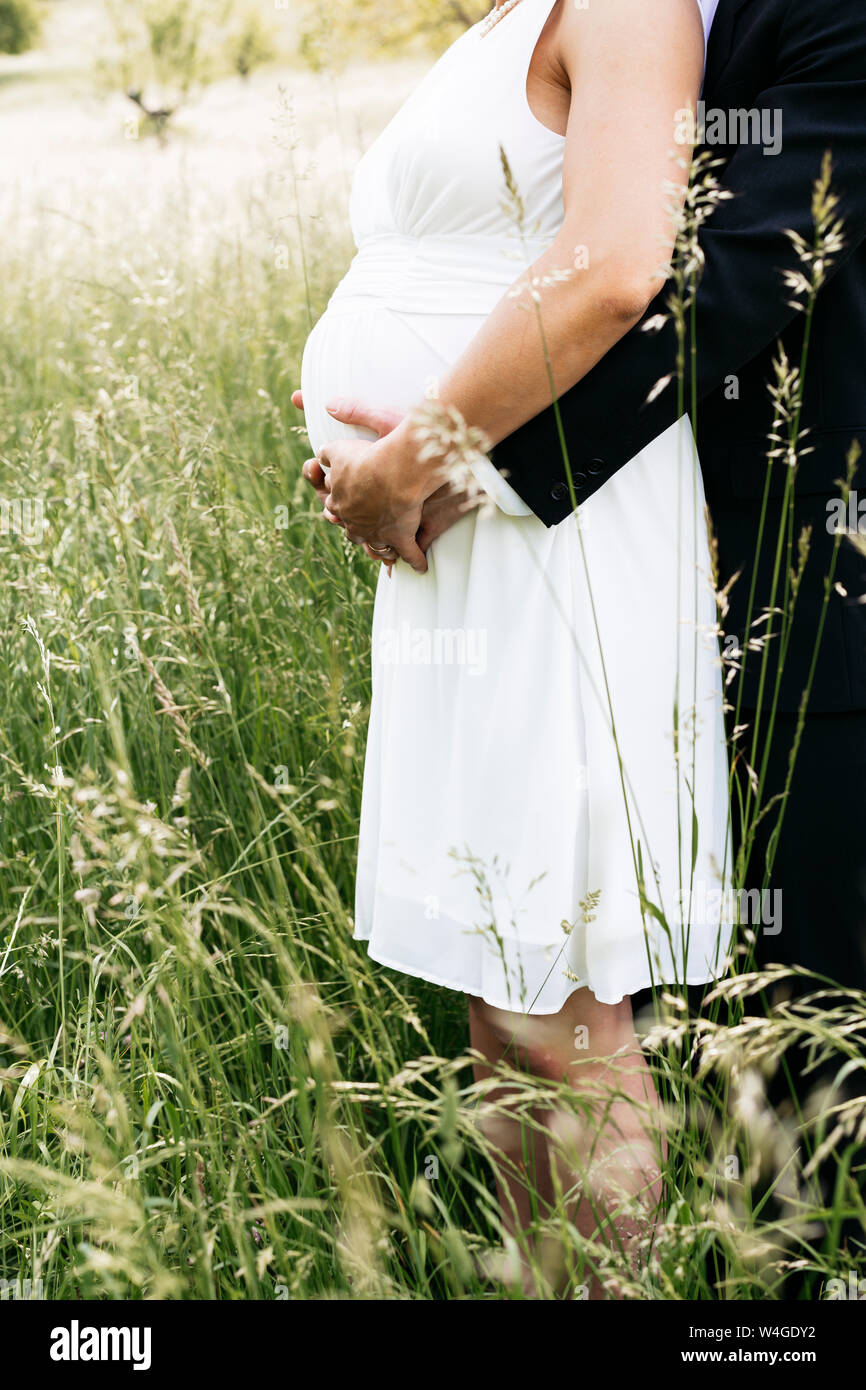 Pregnant bride with her husband holding baby belly on a meadow Stock ...