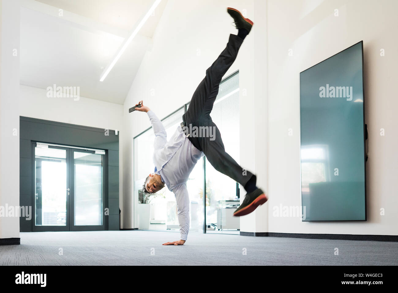 Businessman with cell phone doing a one-handed handstand on office ...