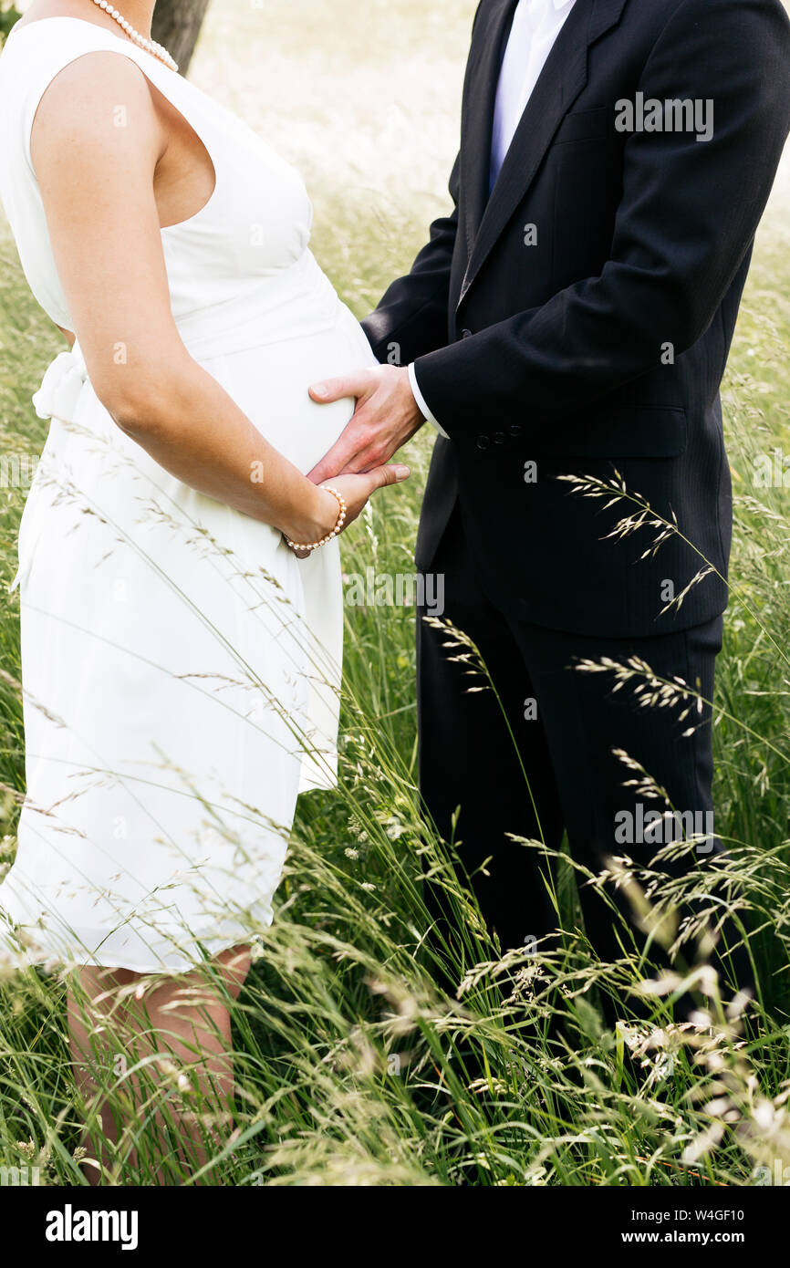 Pregnant bride with her husband holding baby belly on a meadow Stock ...