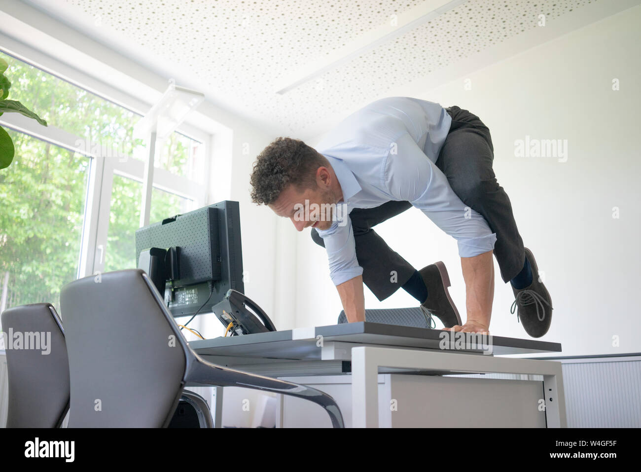 Businessman balancing on desk in office Stock Photo - Alamy