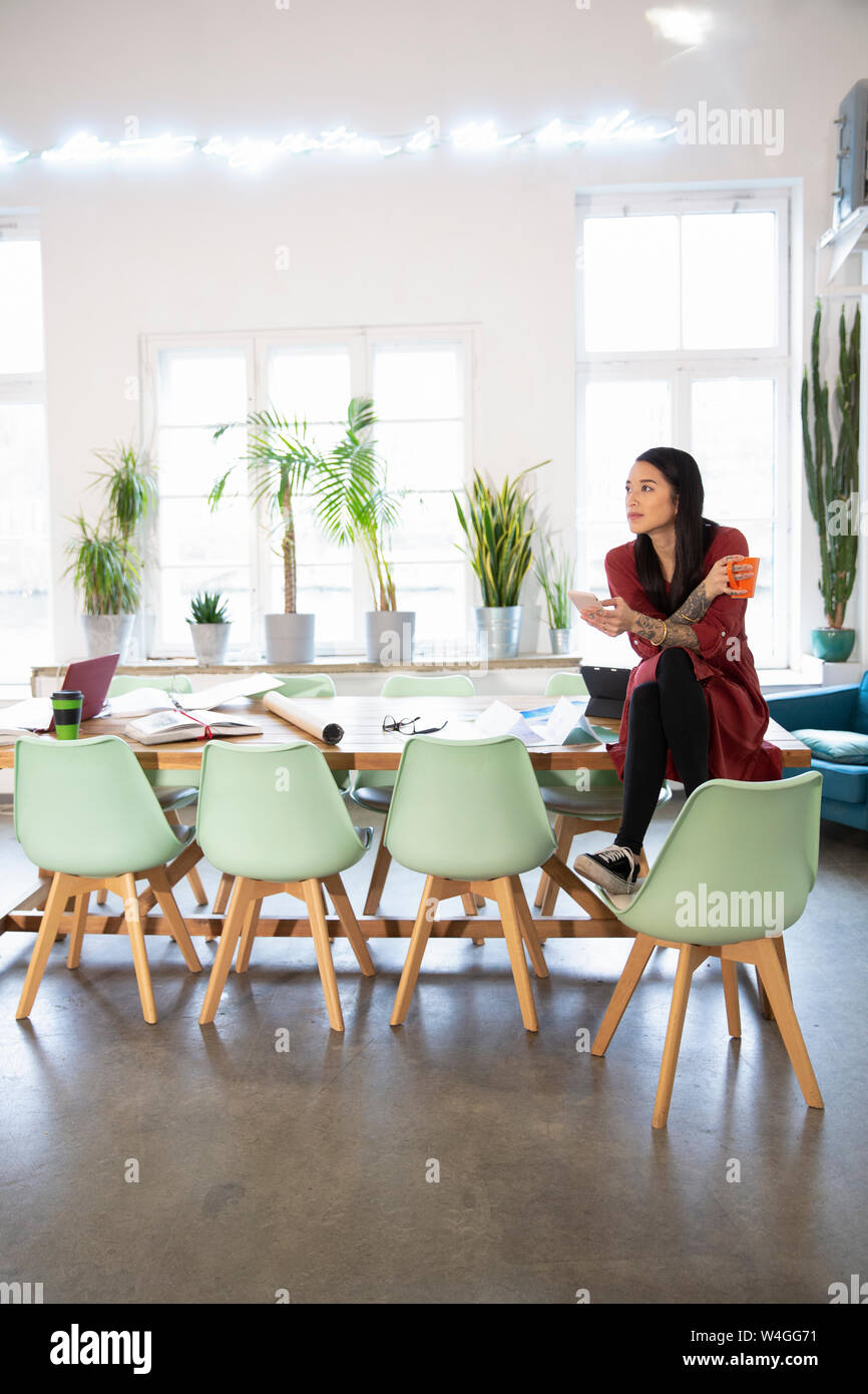 Woman sitting on table in modern office Stock Photo - Alamy