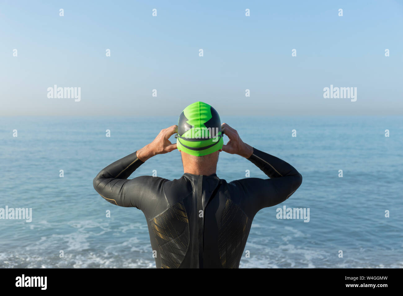 Triathlete preparing to swim, putting on swimming cap and goggles, rear ...