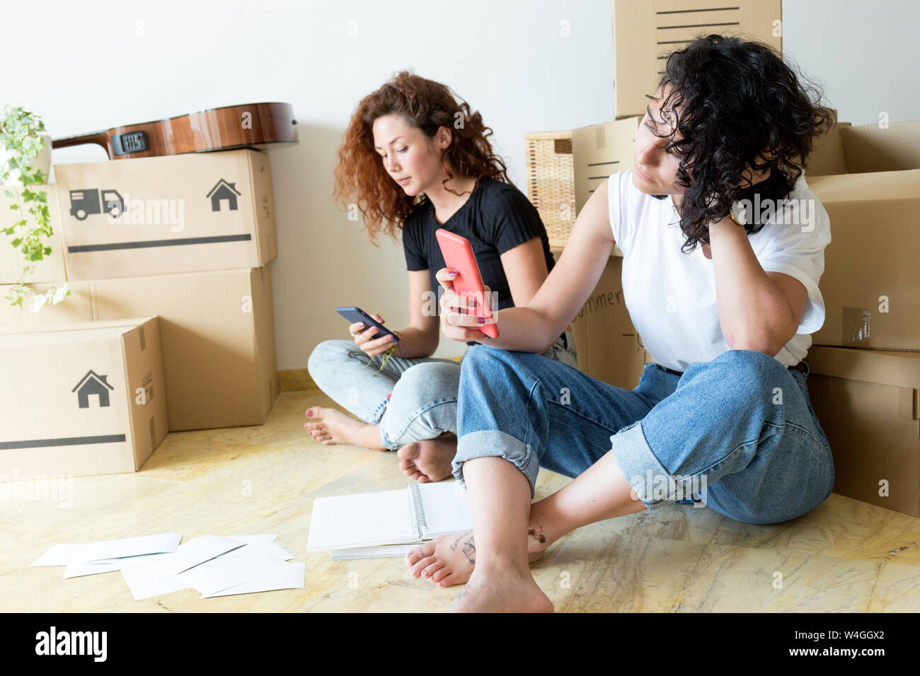Two friends moving into new home using cell phones Stock Photo - Alamy
