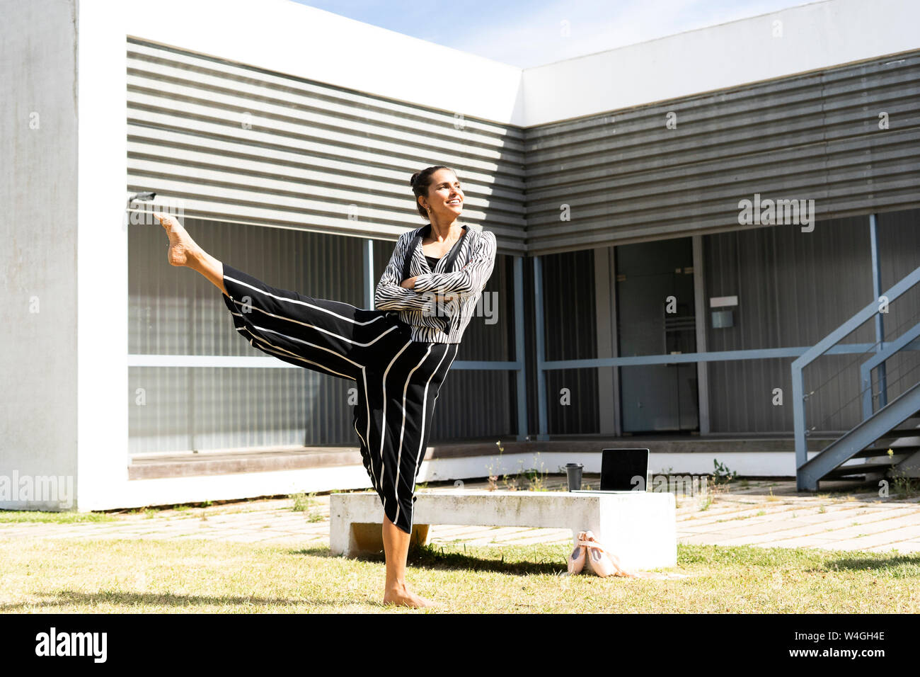 Female ballet dancer lifting her leg in front of an office building ...