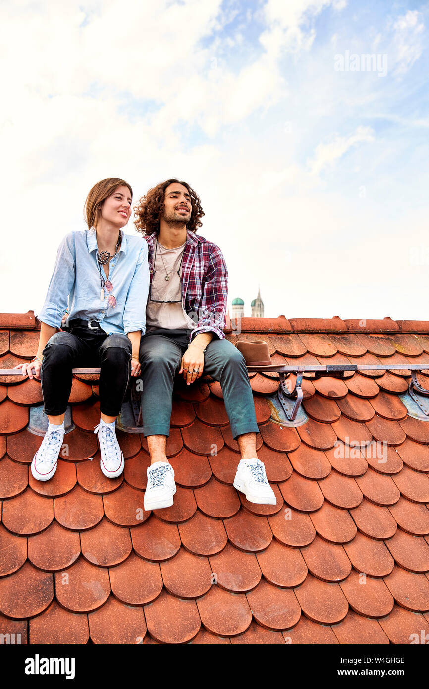Young couple sitting on rooftop and looking at distance Stock Photo - Alamy