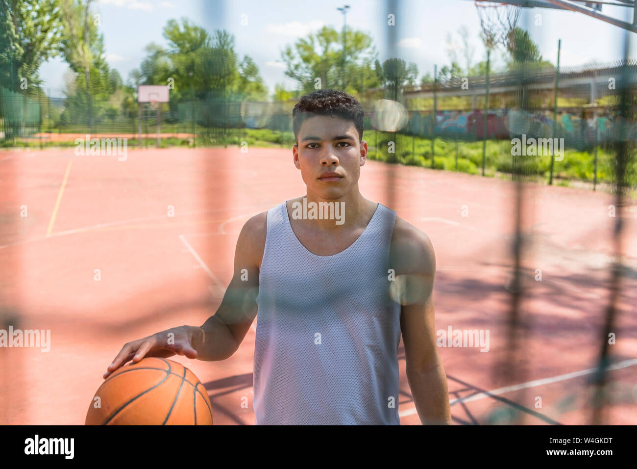 Young man playing basketball looking at camera, behind net Stock Photo ...