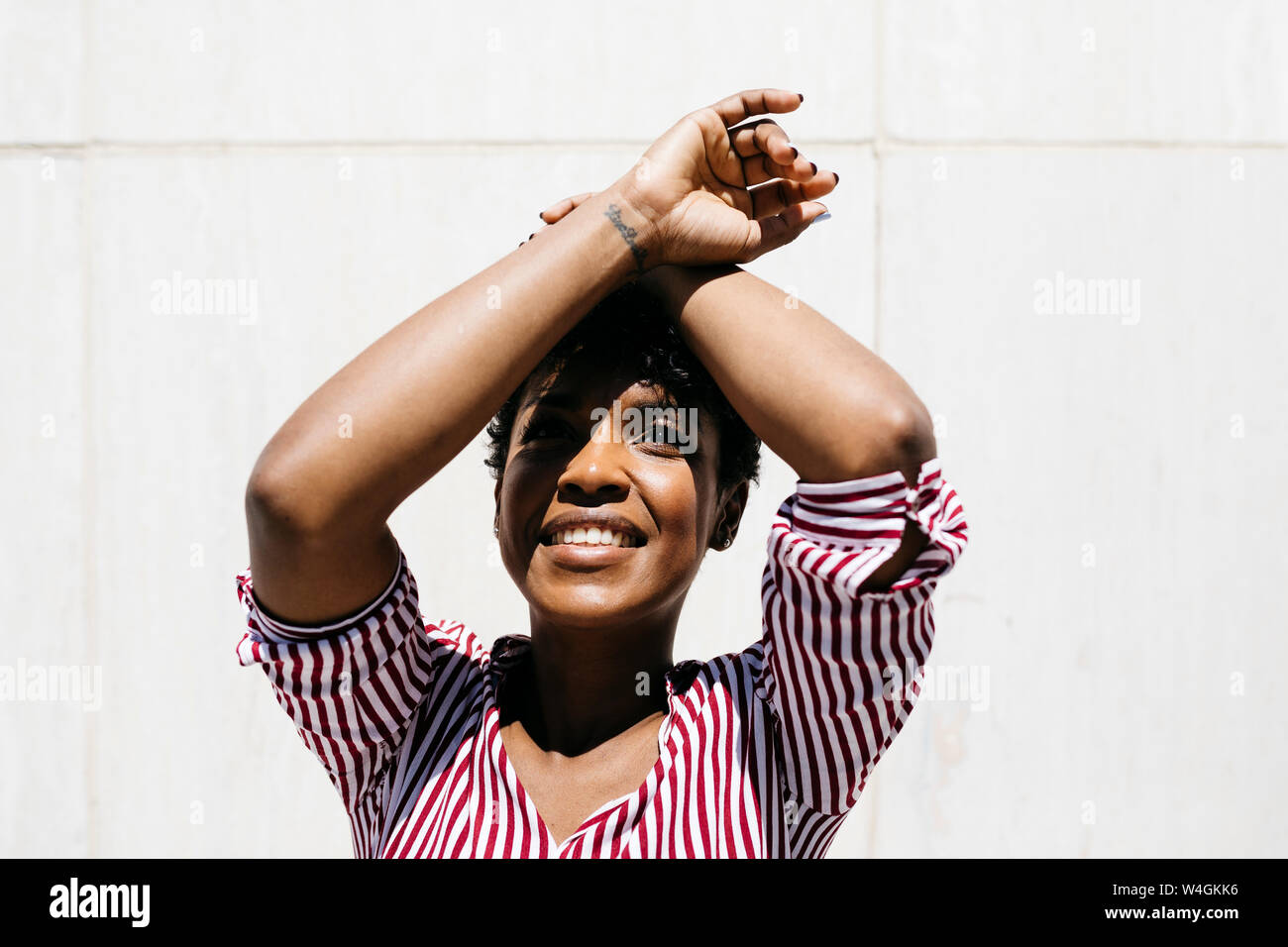 Portrait of woman covering the sun with her arm, white wall in the ...