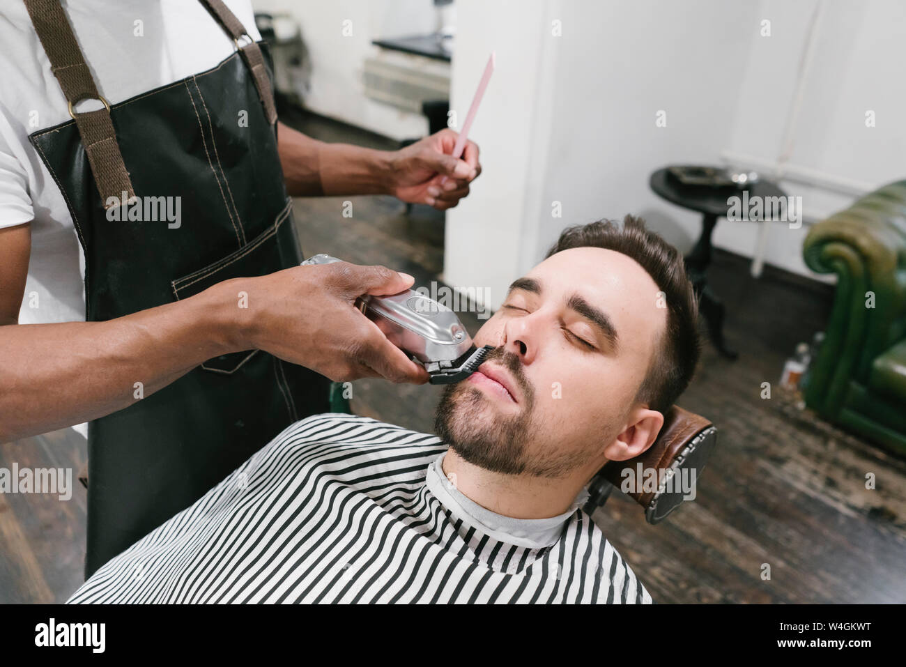 Barber cutting beard of a customer in barber shop Stock Photo - Alamy