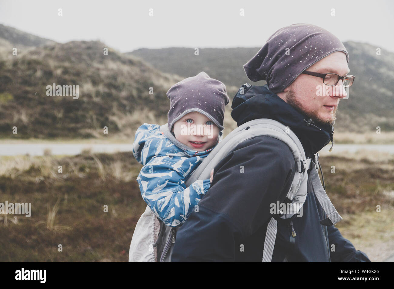 Man carrying his toddler son in baby carrier on his back, Sylt, Germany ...