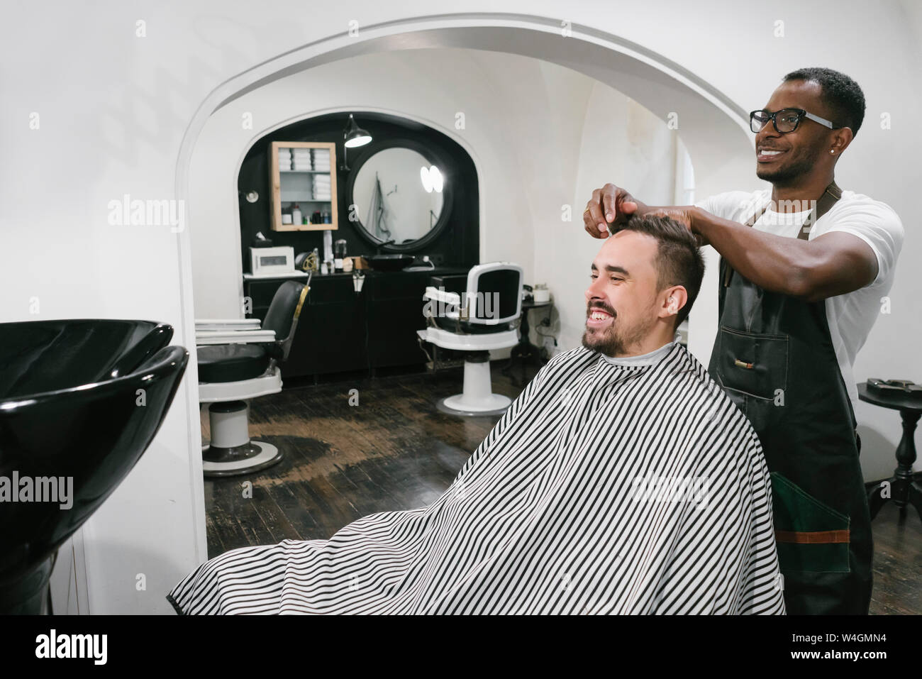 Smiling barber cutting hair of a customer in barber shop Stock Photo ...