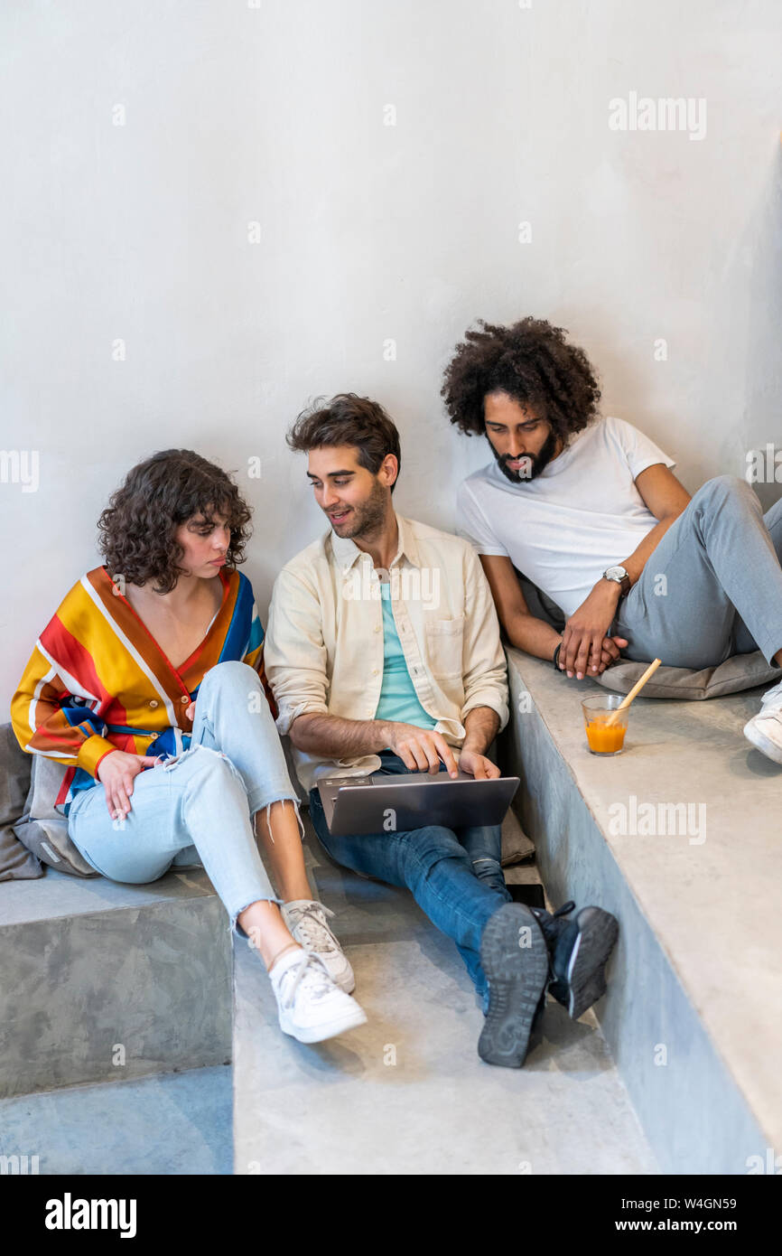 Three friends sitting on stairs with laptop and drink Stock Photo - Alamy