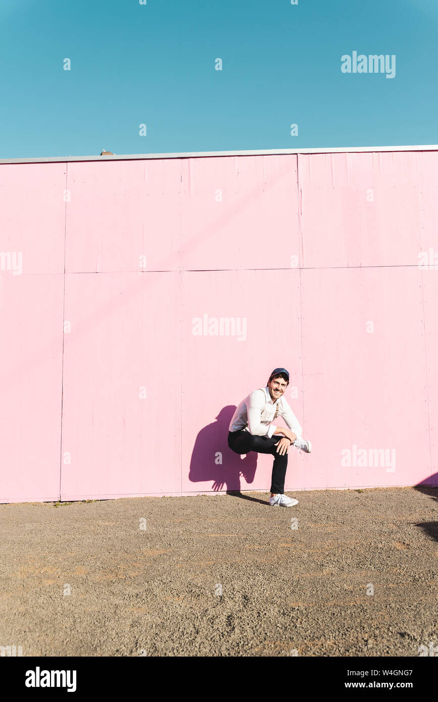 Young man in front of pink construction barrier, crouching in one leg ...
