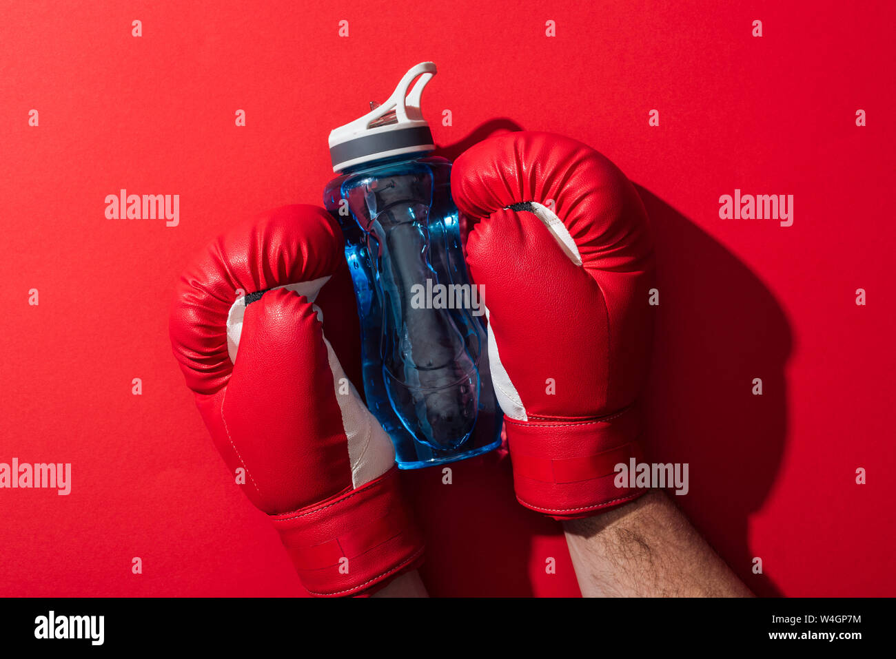 cropped view of boxer holding sport bottle with boxing gloves on red ...