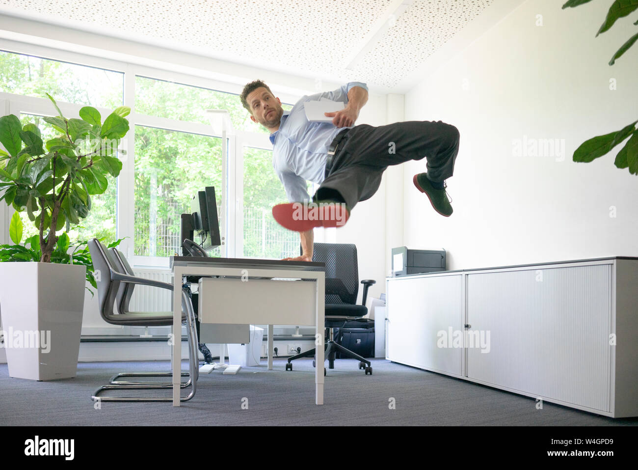 Businessman doing a one-handed handstand on desk in office Stock Photo ...