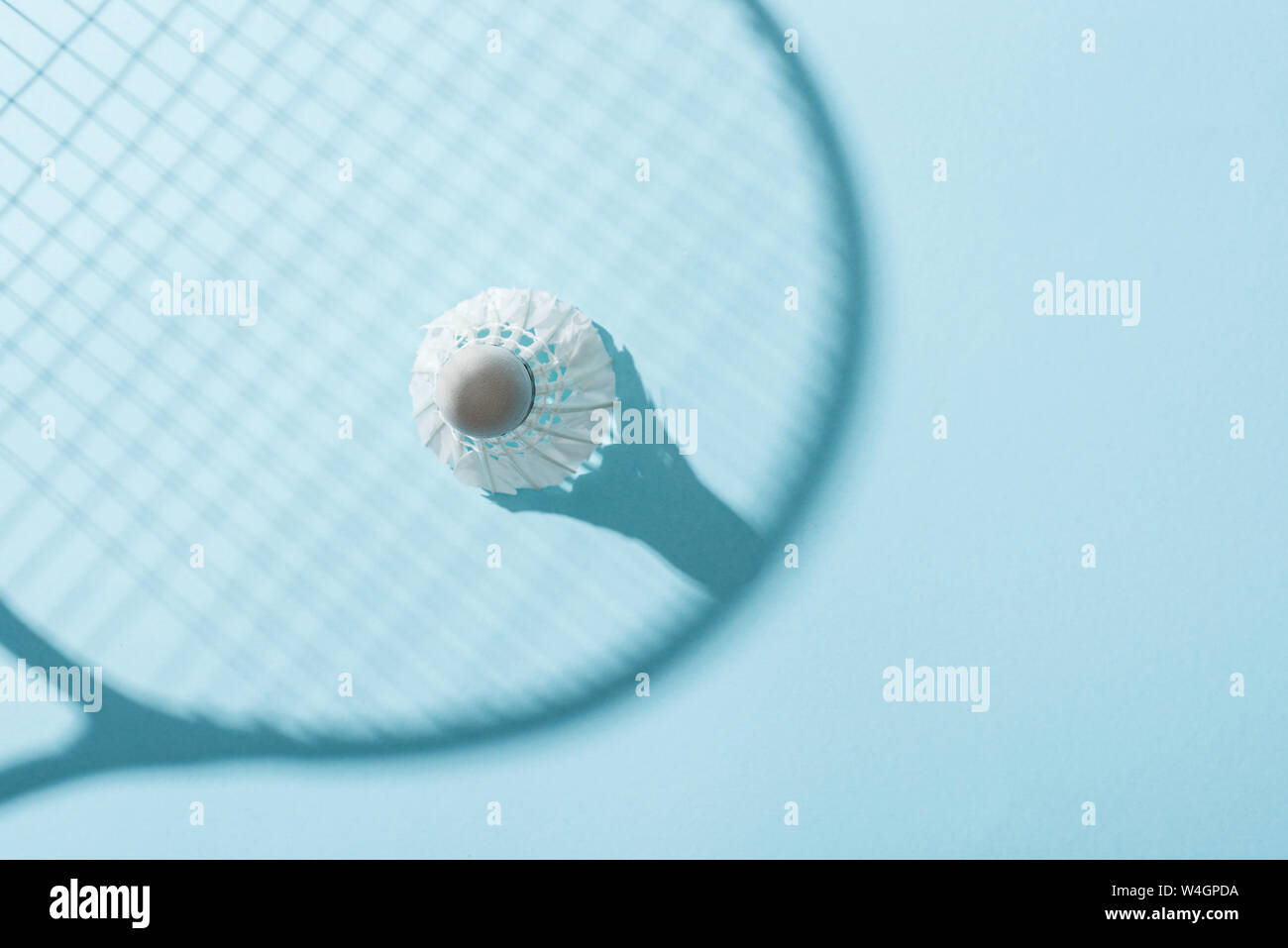 top view of white shuttlecock with feathers near shadow of badminton ...