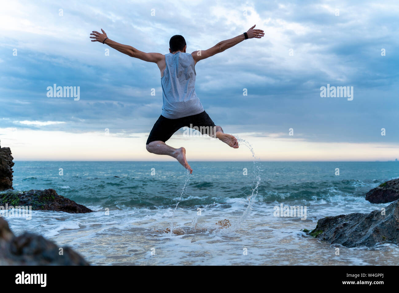 Back view of young man jumping in the air at seafront Stock Photo - Alamy