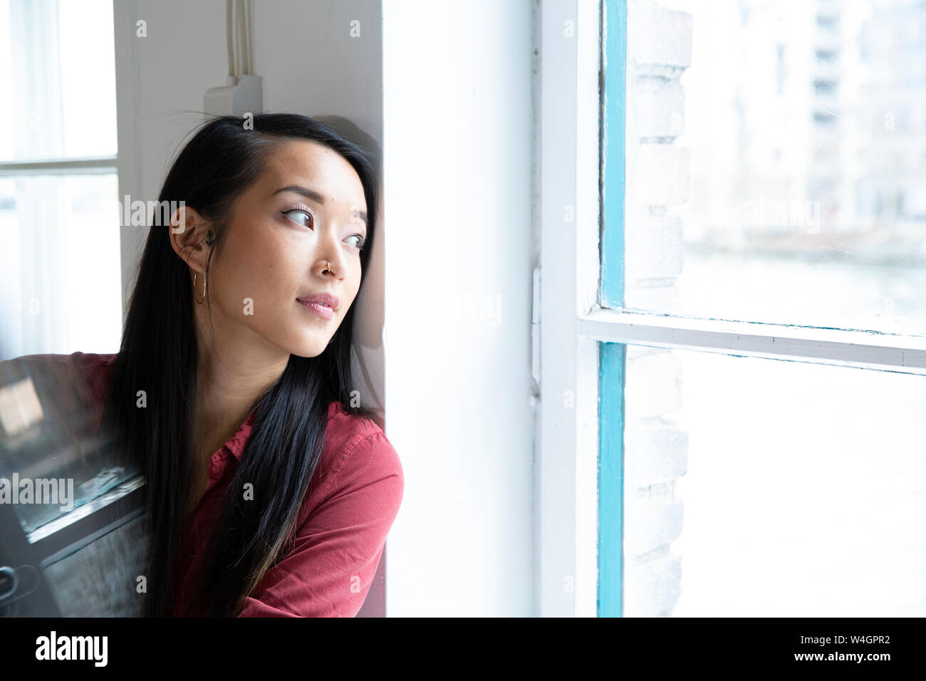 Portrait of woman looking out of window in office Stock Photo - Alamy