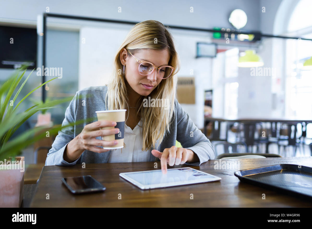 Young woman working with her digital tablet while drinking coffee in ...