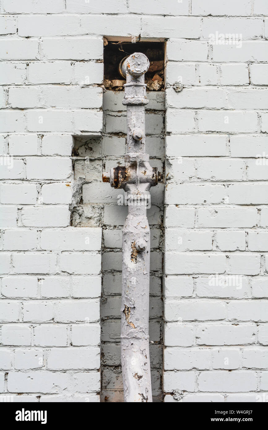 Old rusty pipe with valves on painted white classic brick wall with ...