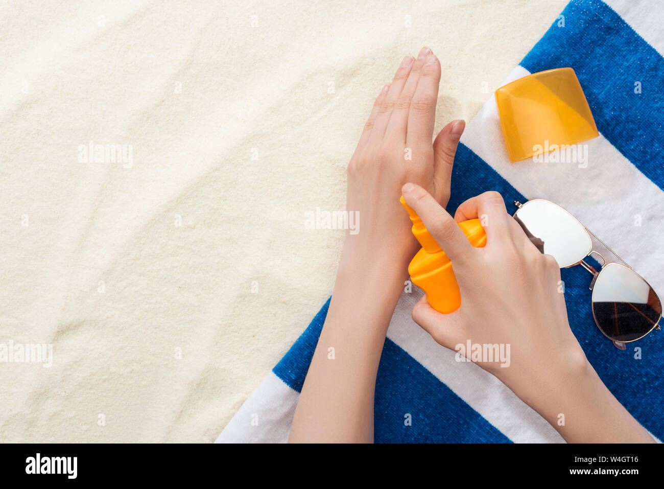 cropped view of woman applying sunscreen on hands near striped towel ...