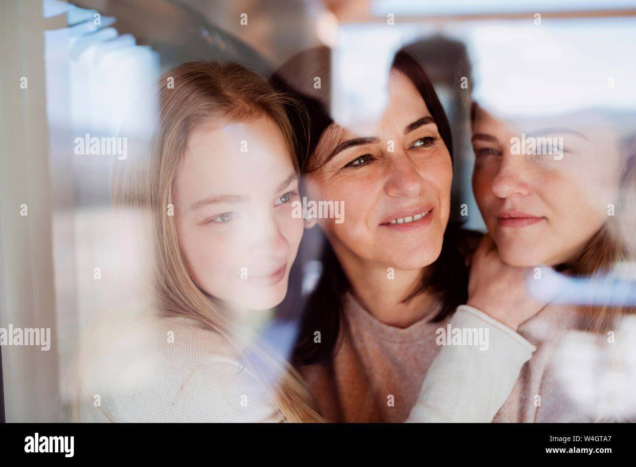 Visiting daughters embracing their mother, standing at the window Stock ...