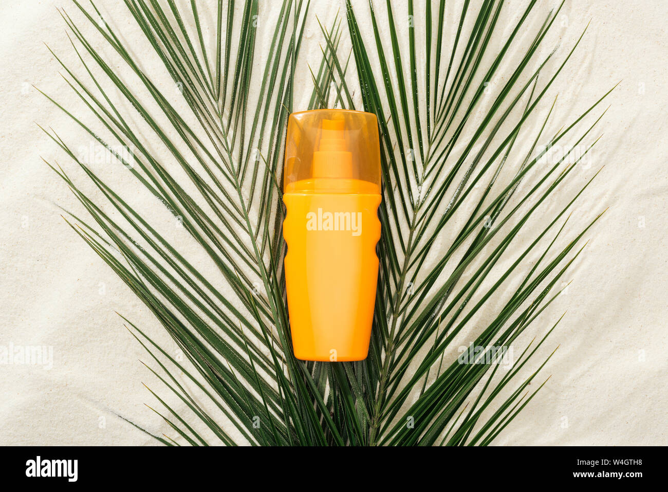 orange sunscreen lotion on green palm leaves on sand Stock Photo - Alamy