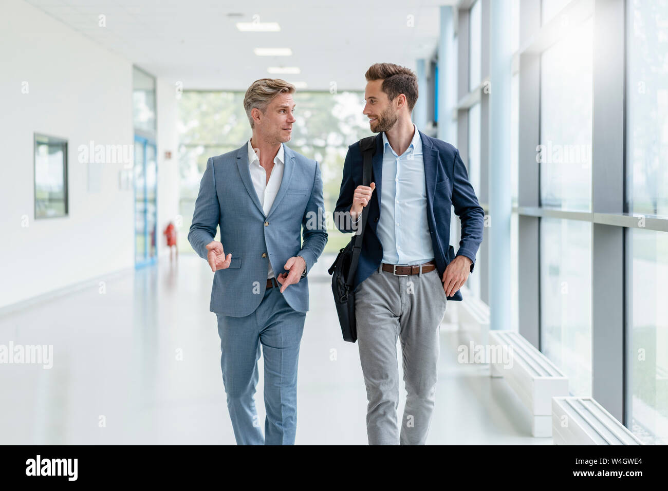 Two businessmen walking and talking in a passageway Stock Photo - Alamy