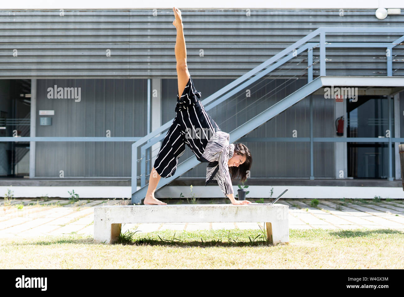 Female ballet dancer lifting her leg on a bench in front of an office ...