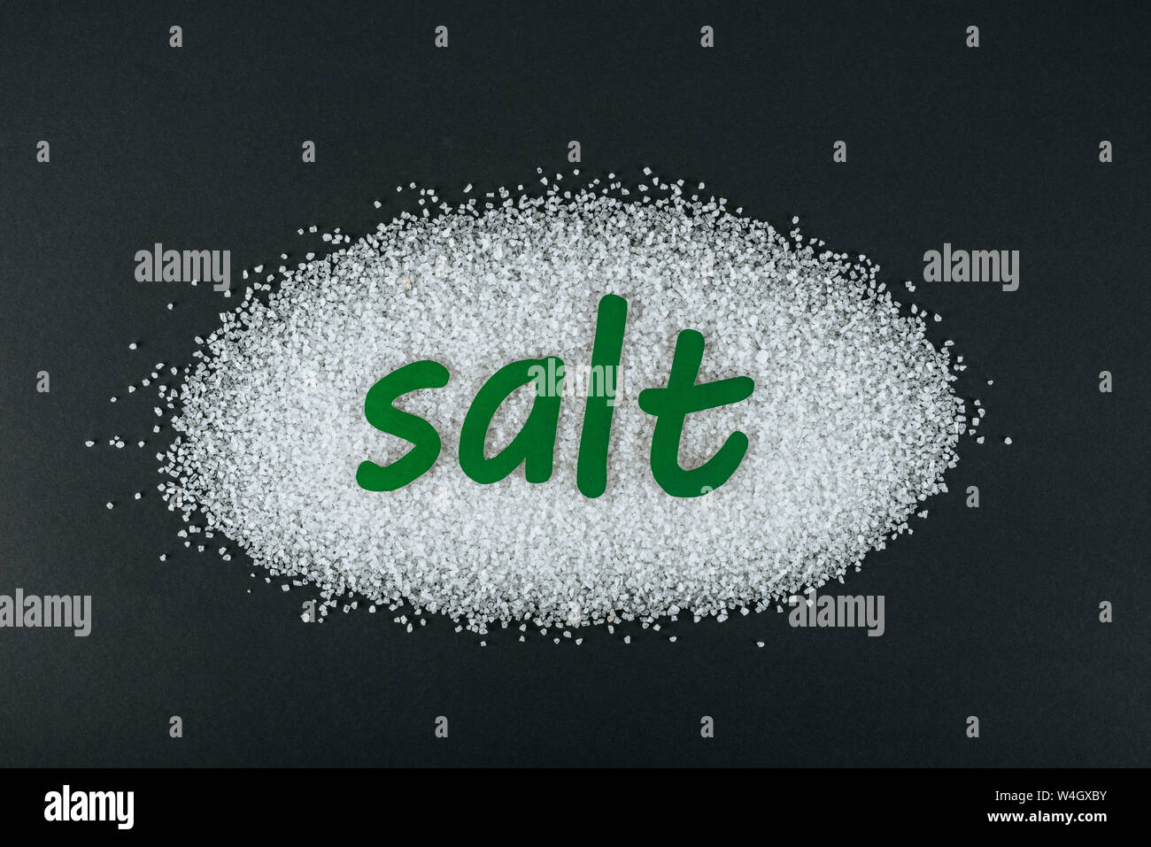 top view of green paper cut word salt on salt crystals on black ...