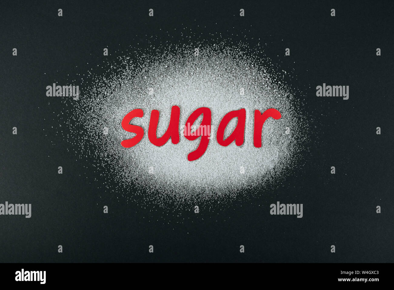 top view of white sugar crystals with red paper cut word sugar on black ...