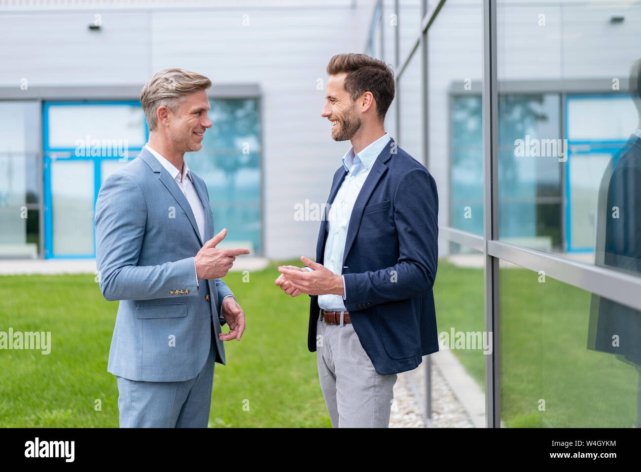 Two smiling businessmen talking outside office building Stock Photo - Alamy